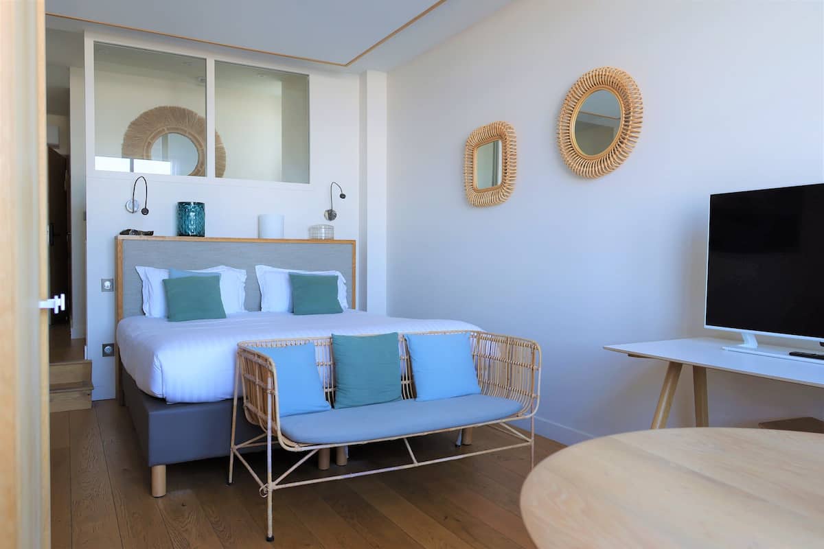 Quarto moderno com cama, mesa de cabeceira, televisão e dois espelhos na parede.