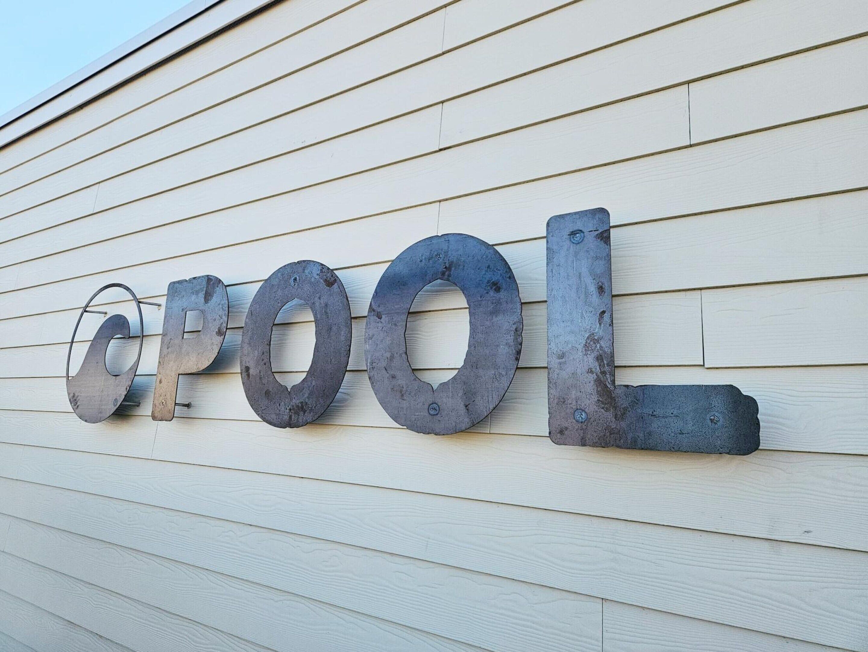 Um letreiro de metal com as letras 'CPOOL' fixado numa parede de madeira.