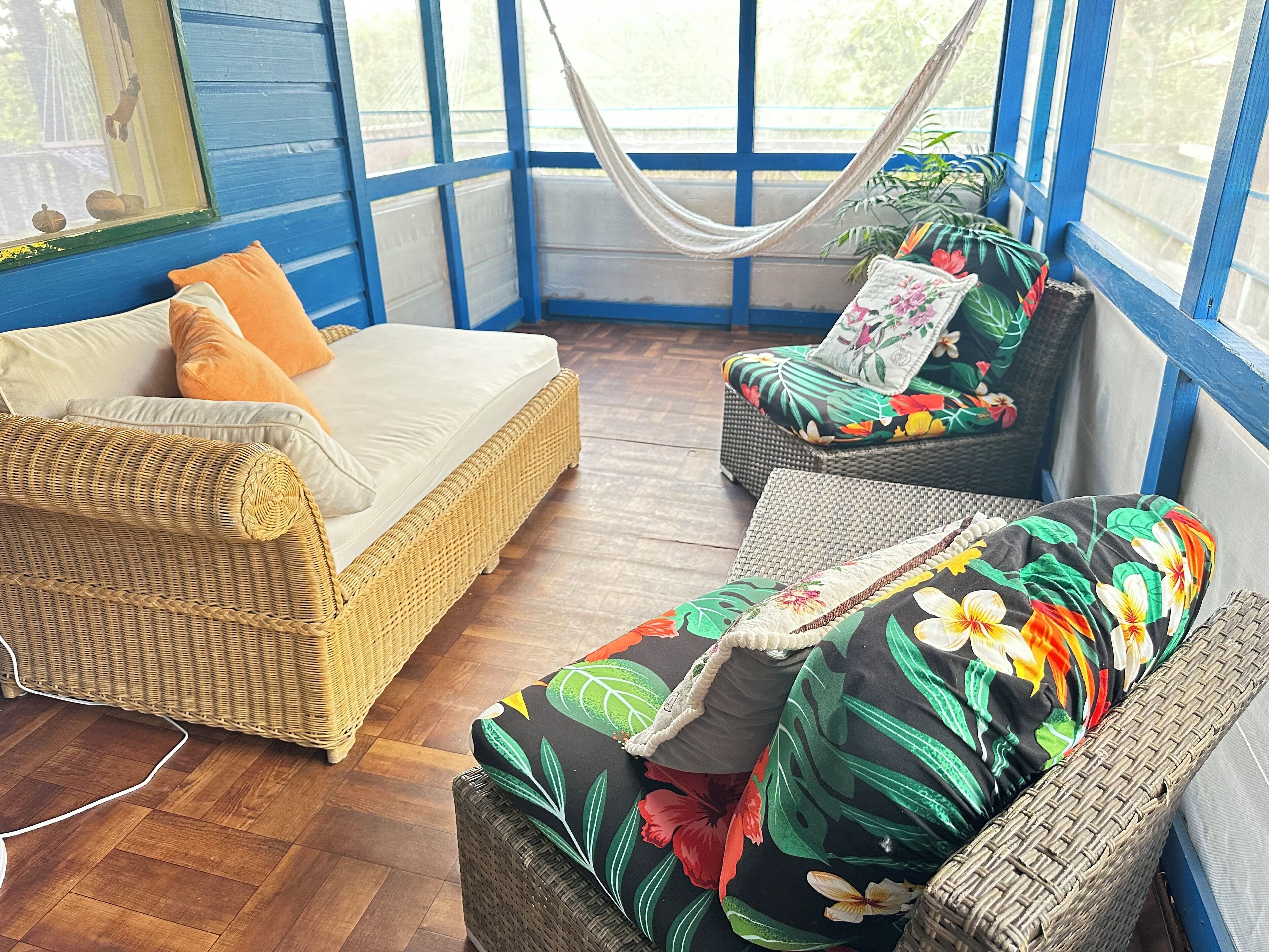 Um quarto com um sofá de vime, uma poltrona acolchoada e uma rede.