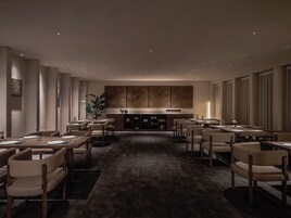 Uma ampla área de refeições com várias mesas e cadeiras, uma cozinha central e um grande quadro abstrato na parede.