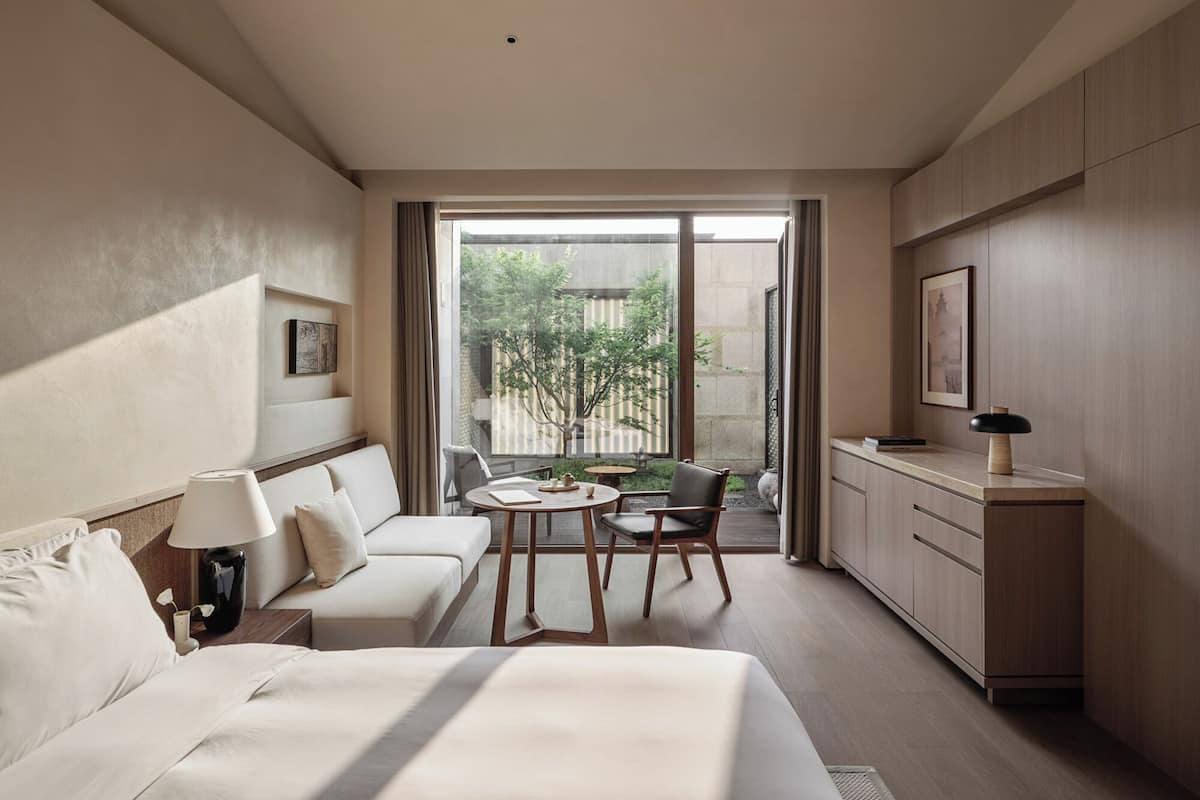 Quarto de hotel com cama, sofá, escrivaninha e vista para um pátio.