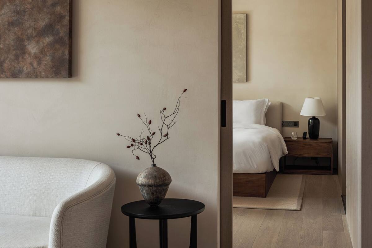 Quarto de hotel moderno com uma cama grande, uma mesinha de cabeceira com um vaso, um criado-mudo com abajur e um quadro na parede.