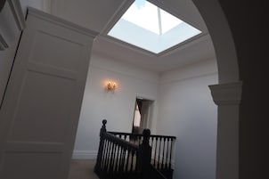 Escadaria com claraboia que leva a um segundo andar, luminária fixada na parede e uma porta no topo das escadas.
