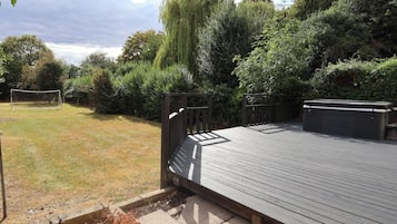 Um deck de madeira com guarda-corpo de metal, rodeado por um jardim com diversas plantas e uma árvore.