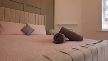 Cama bem arrumada com colcha rosa, cabeceira e duas almofadas.