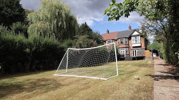 Um gol de futebol numa área gramada com uma casa de tijolos ao fundo.