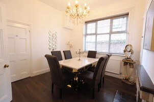 Uma sala de jantar com mesa de mármore, cadeiras escuras, um candeeiro e uma janela com persianas.