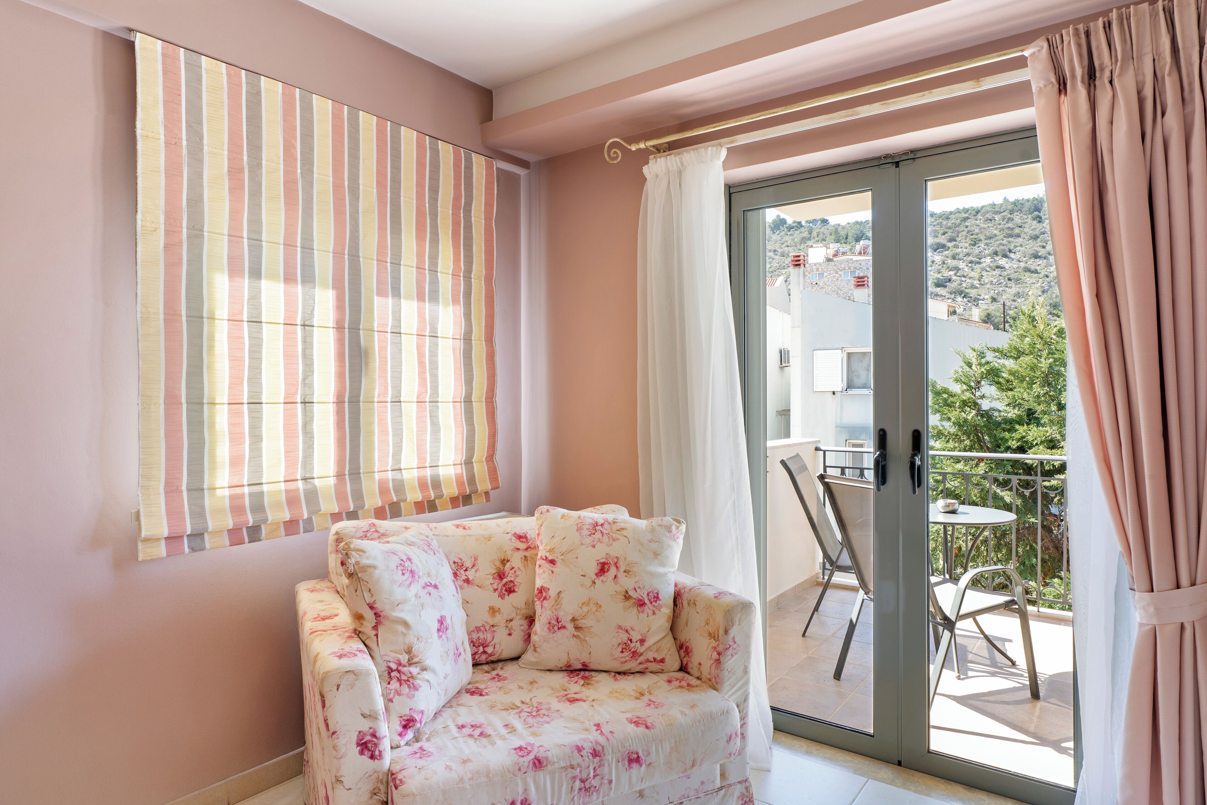 Um quarto aconchegante com um sofá floral, uma cortina listrada e uma varanda com mesa e cadeiras.