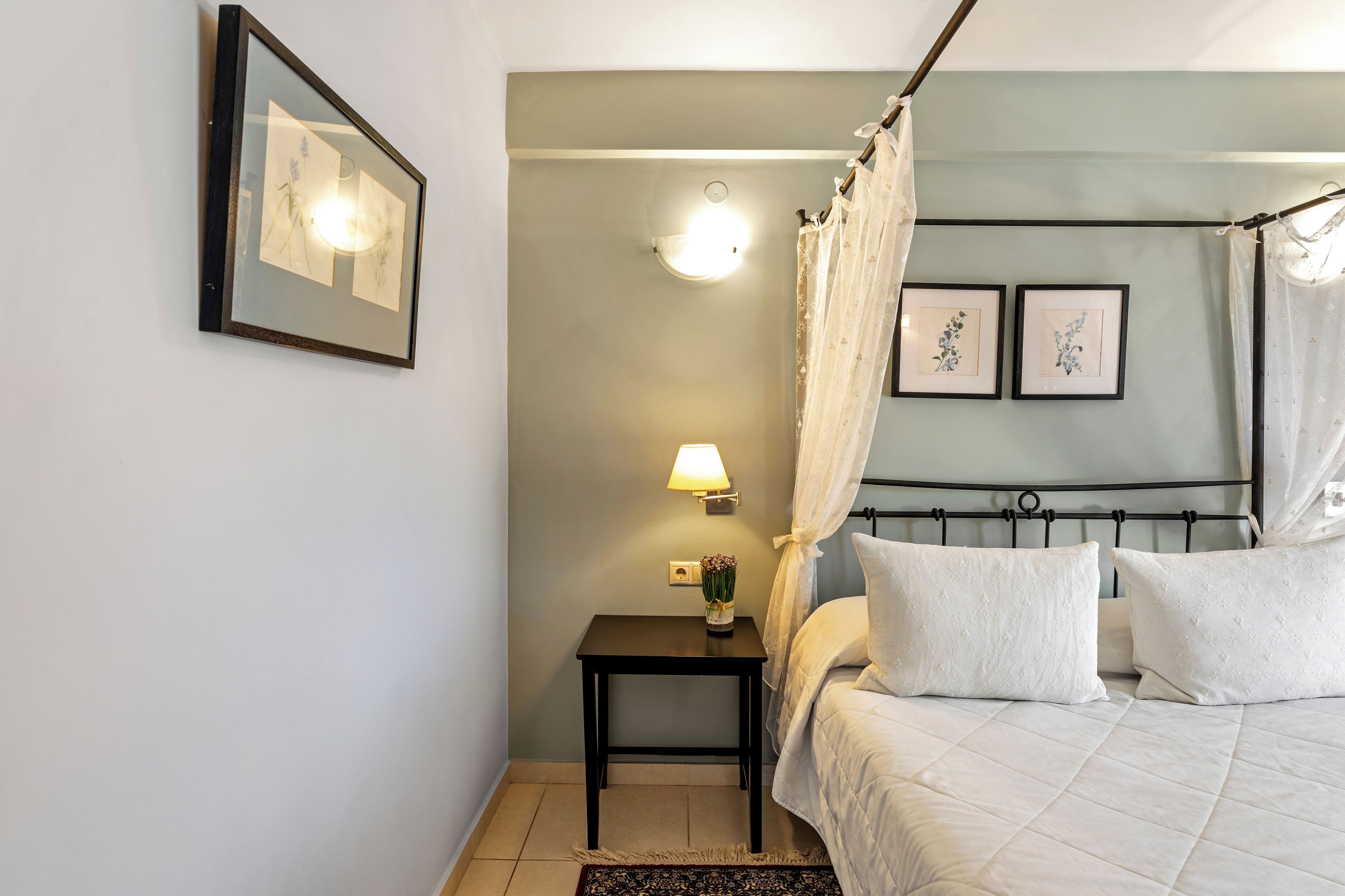 Quarto com cama, mesa de cabeceira, luminária e quadros nas paredes.