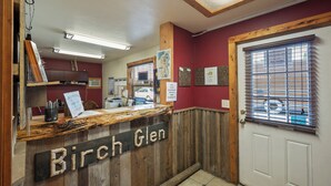 Uma mesa de recepção com a placa "Birch Glen", design em madeira, um mapa na parede e uma janela com persianas.