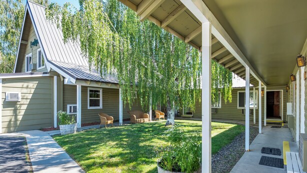 Uma área externa coberta com gramado, assentos e um edifício com telhado inclinado.