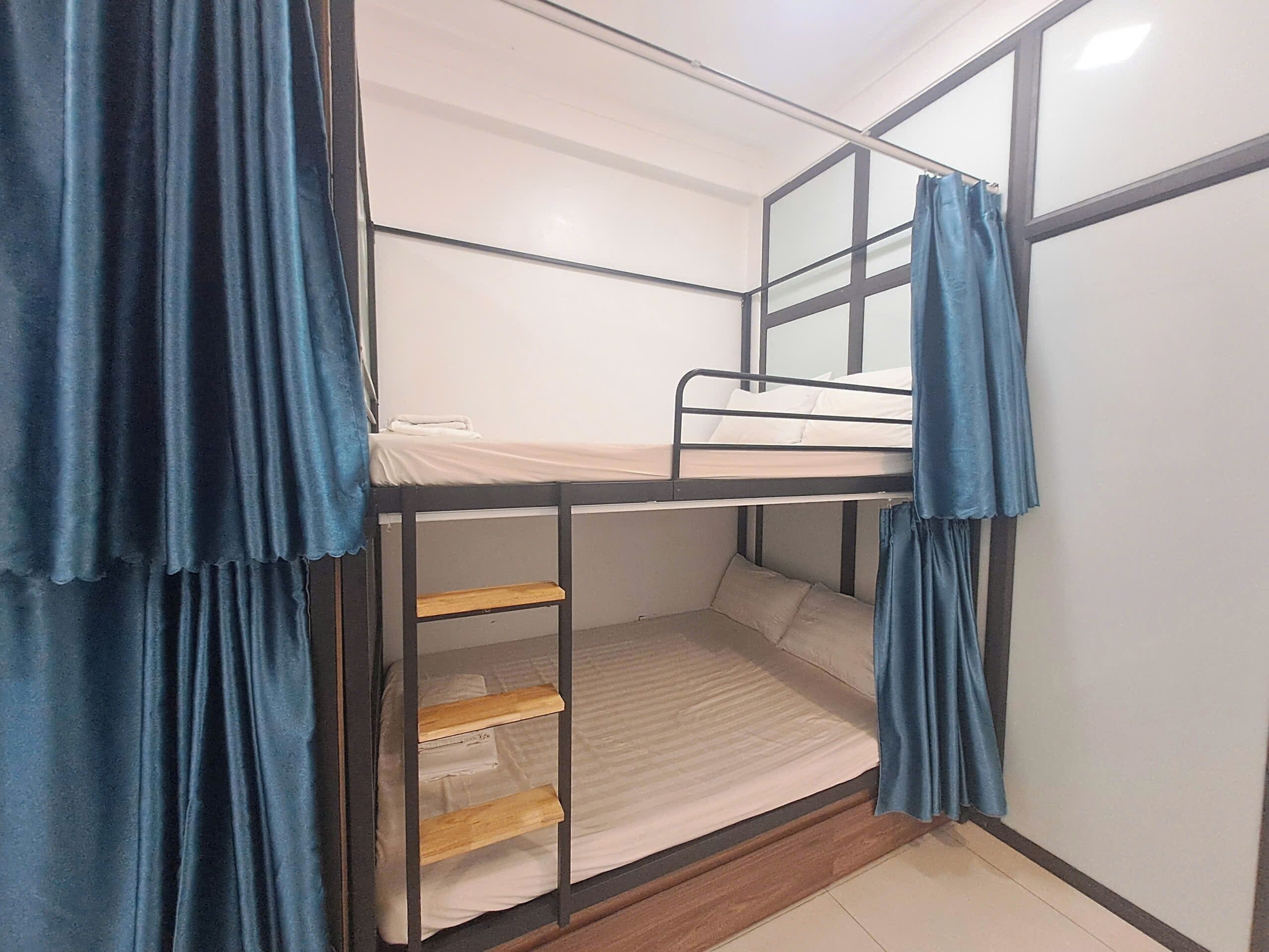 Quarto com beliche, janela, cortinas e prateleira de madeira.