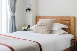 Uma cama bem arrumada com cabeceira de madeira, um travesseiro com texto e uma pequena mesa de cabeceira com um vaso de flores.