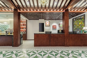 Uma área de recepção com um balcão de madeira, piso estampado e parede com decorações geométricas coloridas.