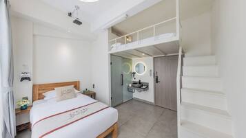 Quarto moderno com uma cama grande, escrivaninha embutida, toucador com espelho e escada para um andar superior.