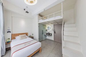 Quarto moderno com uma cama grande, escrivaninha embutida, toucador com espelho e escada para um andar superior.