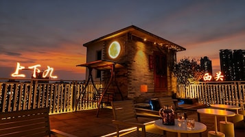 A rooftop bar with a small stone building, outdoor seating, and illuminated signage.
