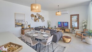 Uma sala de estar moderna com área de jantar, sofá, TV e arte decorativa nas paredes.