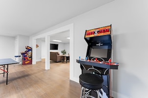 Quarto com mesa de pingue-pongue, jogo de basquete eletrônico e um banquinho de bar.