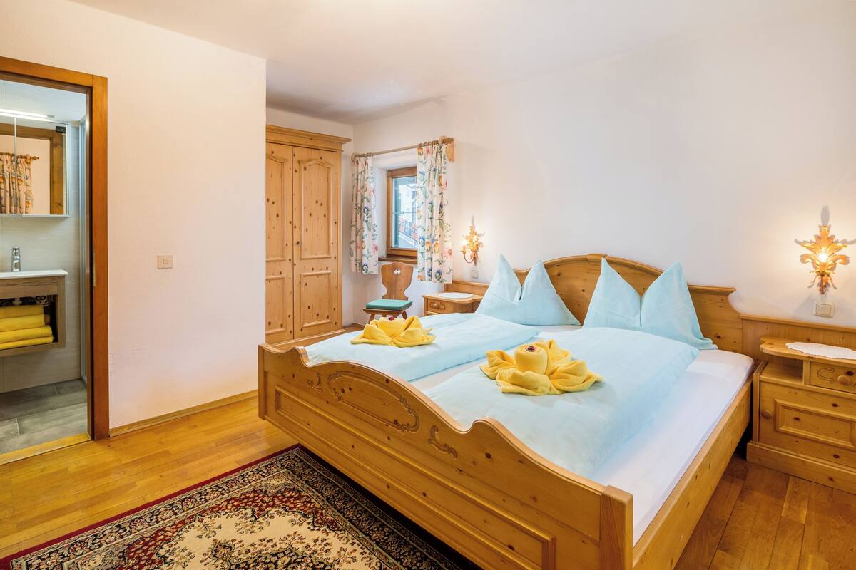 Uma cama de madeira com colcha azul clara, duas almofadas e uma toalha decorativa.