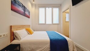 Quarto de hotel com cama, televisão, janela e um quadro na parede.
