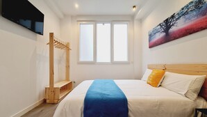 Um quarto com cama, um banco de madeira e um quadro na parede.