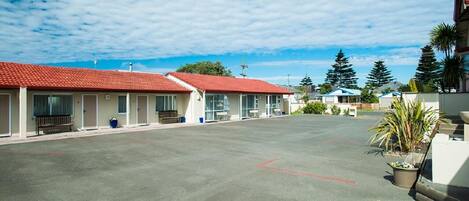 Uma fileira de edifícios de motel com telhados vermelhos, um estacionamento e alguma vegetação.