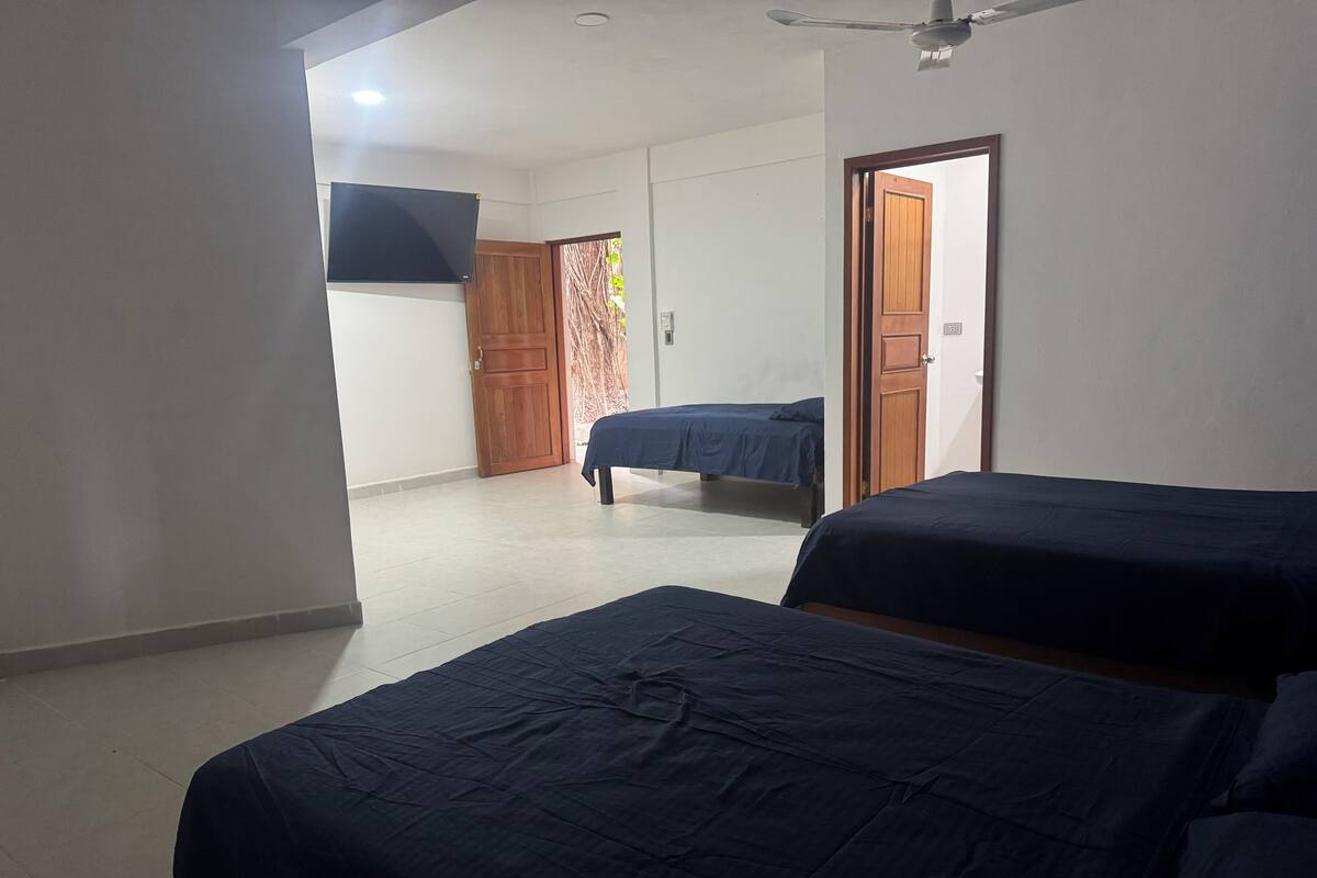 Quarto com duas camas, um ventilador de teto e uma porta que dá para outro cômodo.