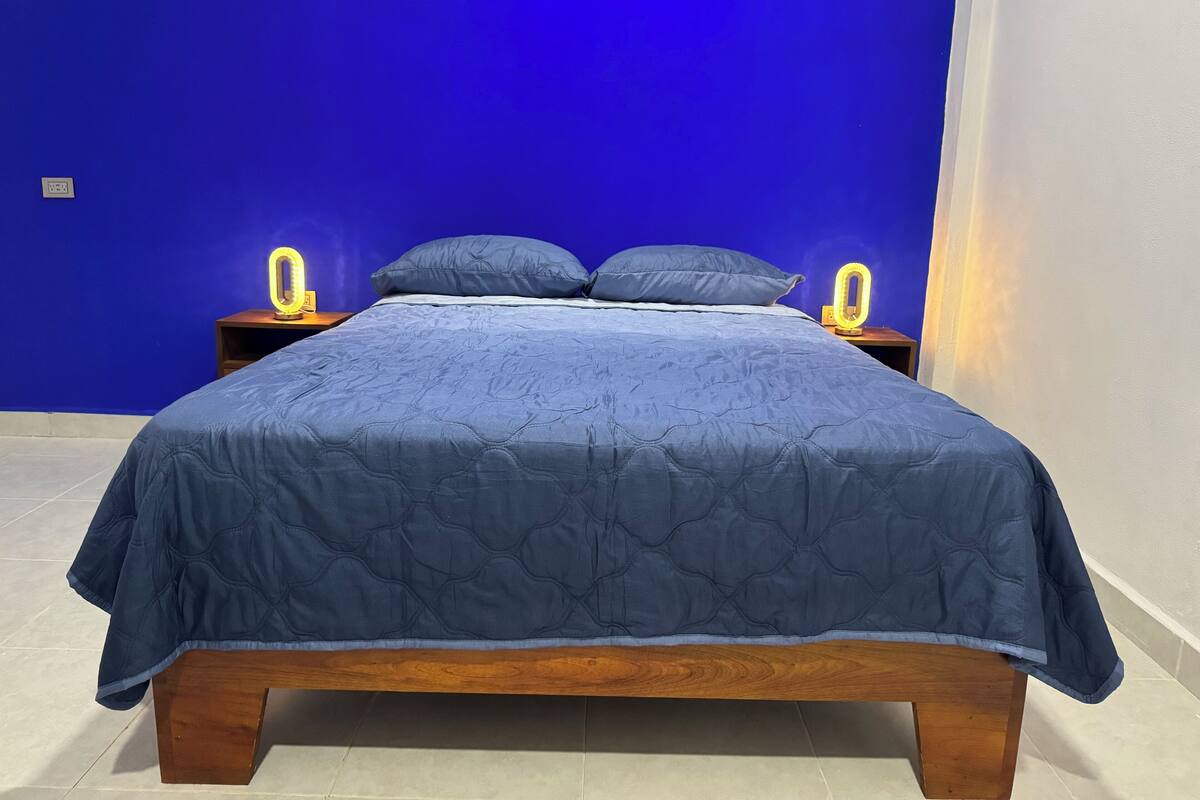 Uma cama com um edredom azul, duas mesas de cabeceira com espelhos iluminados e uma parede azul.