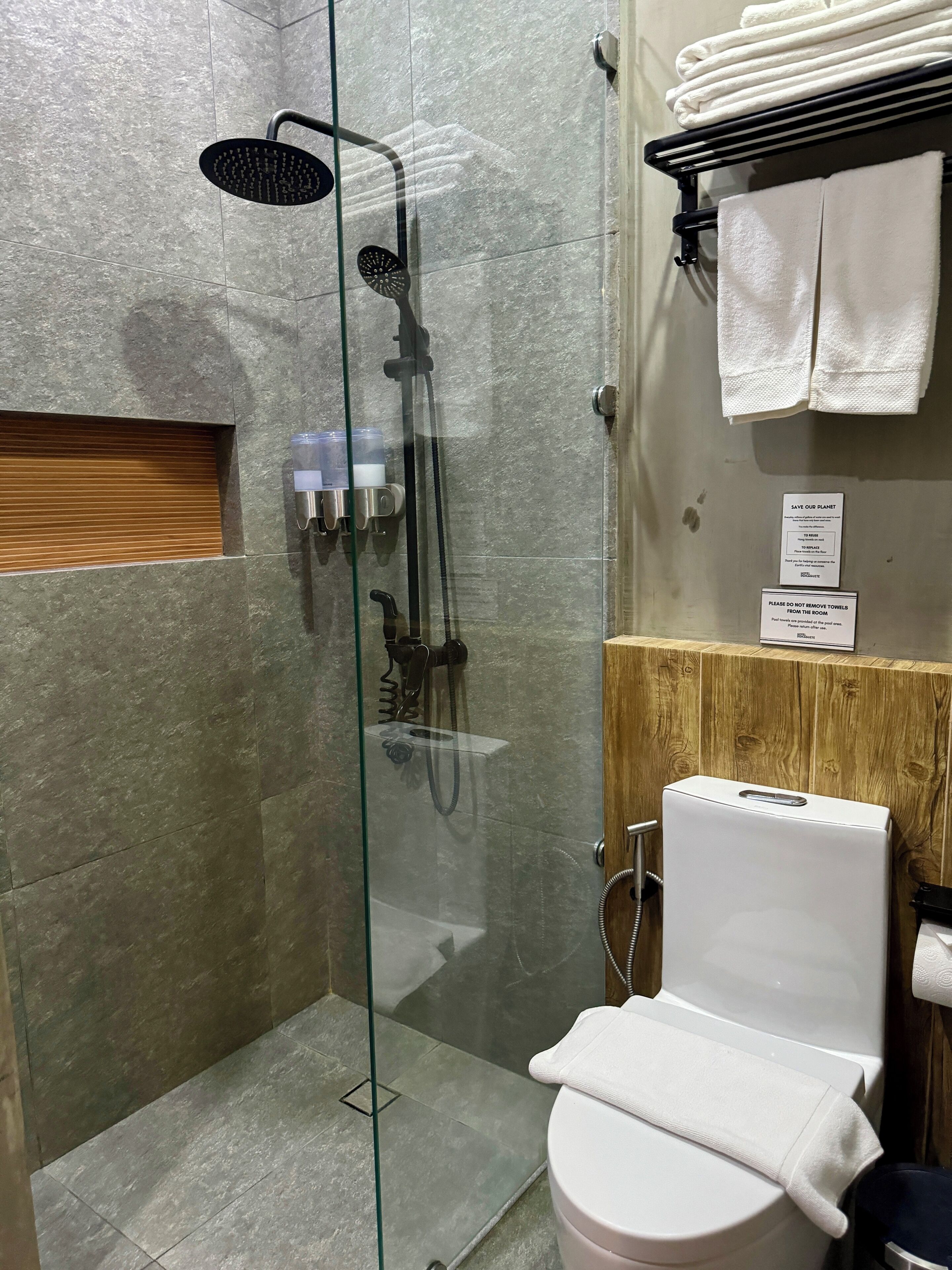 Casa de banho moderna com chuveiro envidraçado, sanita e porta-toalhas com toalhas dobradas.
