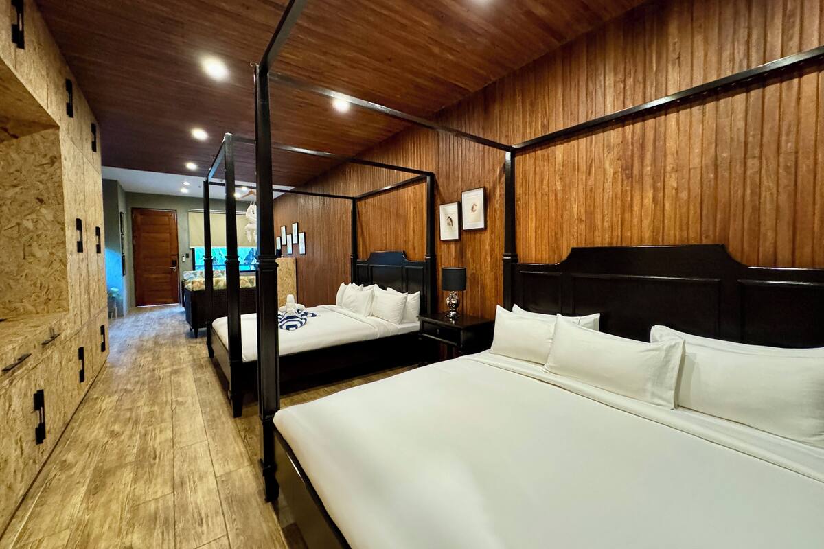 Uma cama de dossel com roupa de cama branca, soalho de madeira e parede revestida a madeira com molduras de quadros.