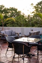 Um pátio externo com móveis de vime, uma mesa de vidro e vista para árvores.