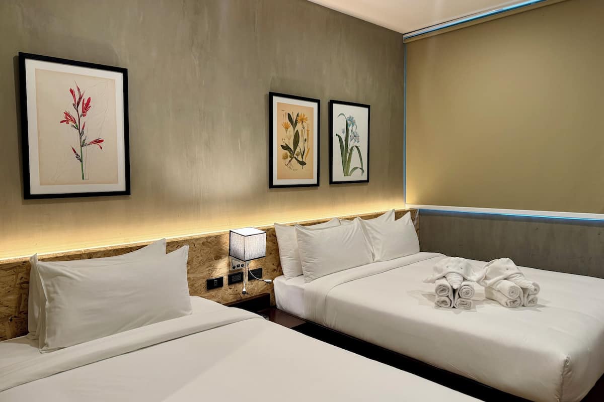 Quarto de hotel com duas camas, uma mesinha de cabeceira e obras de arte fixadas na parede.