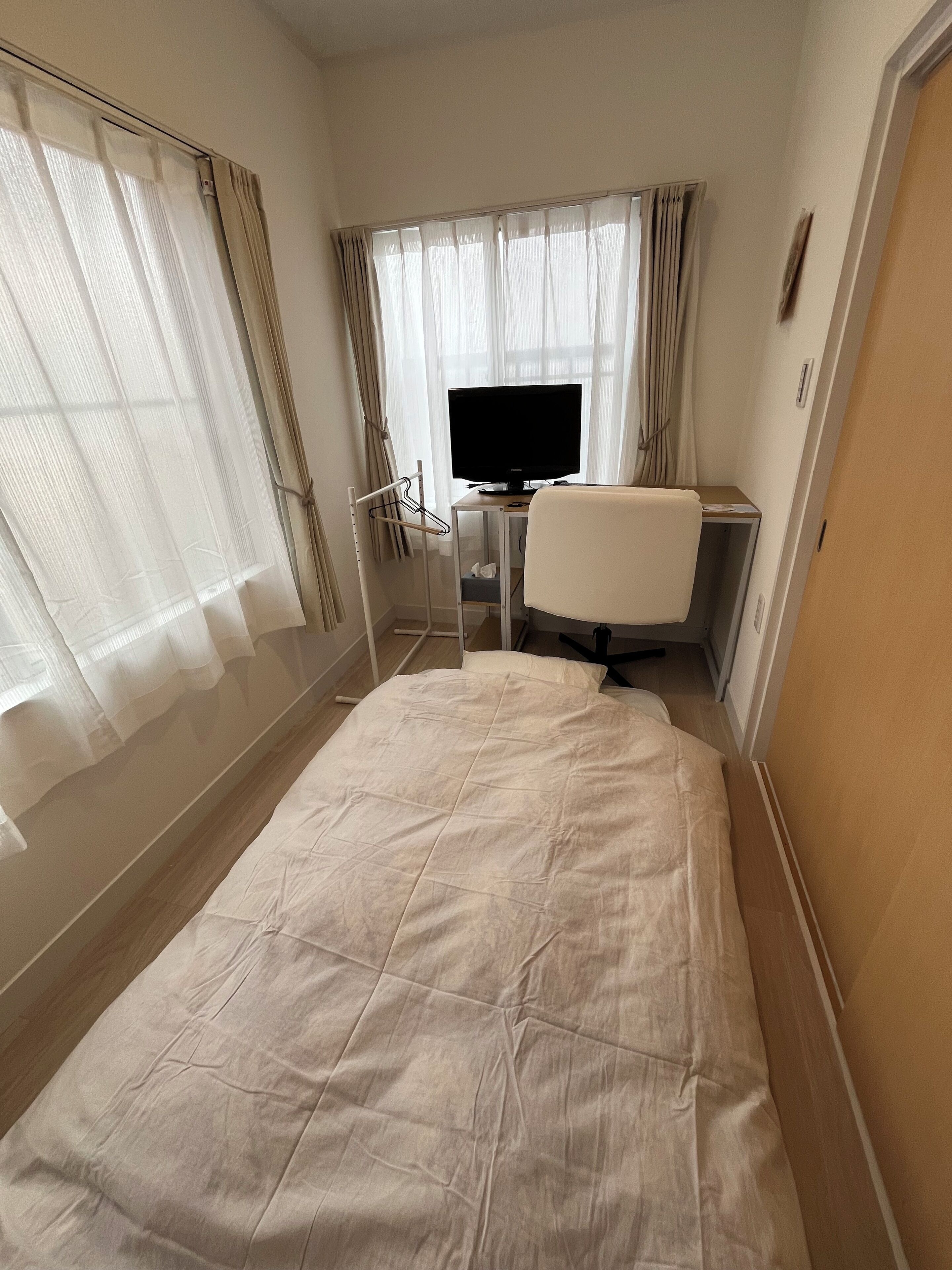 Quarto de hotel com cama, televisão, cadeira e cortinas.
