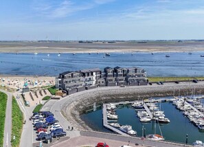 Uma marina costeira com vários barcos atracados, um estacionamento com carros e um edifício com varandas com vista para a água.