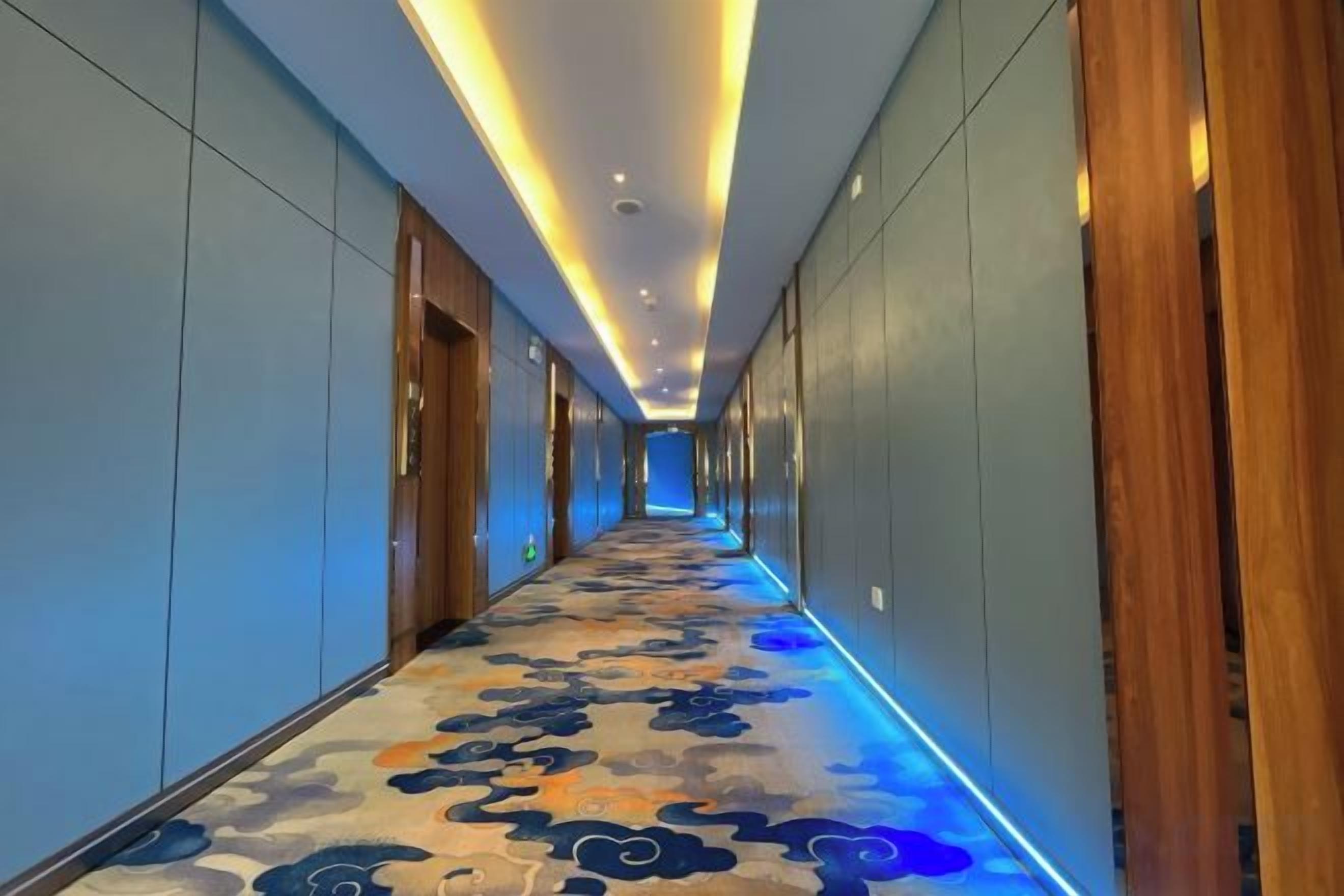Corredor de hotel com carpete estampado, portas de madeira e iluminação embutida.