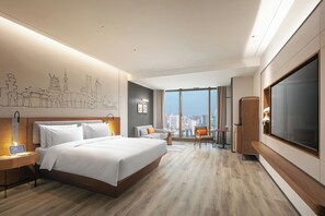 Quarto de hotel moderno com uma cama grande, uma escrivaninha com um laptop, uma televisão e vista para a cidade.