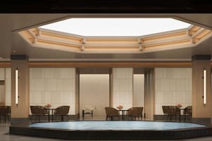 Amplo espaço interno com piscina central, áreas de estar e alto teto com claraboias.