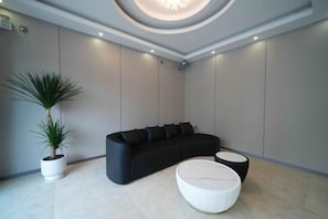 Um interior moderno com um sofá preto, um banquinho redondo branco e uma planta em vaso.