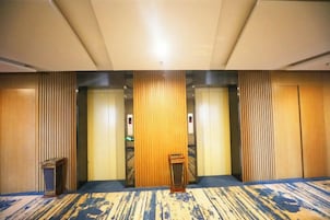 Corredor de hotel com piso carpetado, painéis de madeira e balcão de recepção.