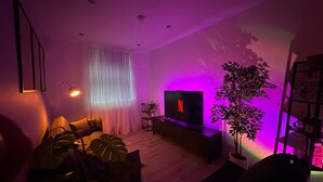 Sala de estar com televisão de tela plana, sofá, mesa de centro e planta em vaso.