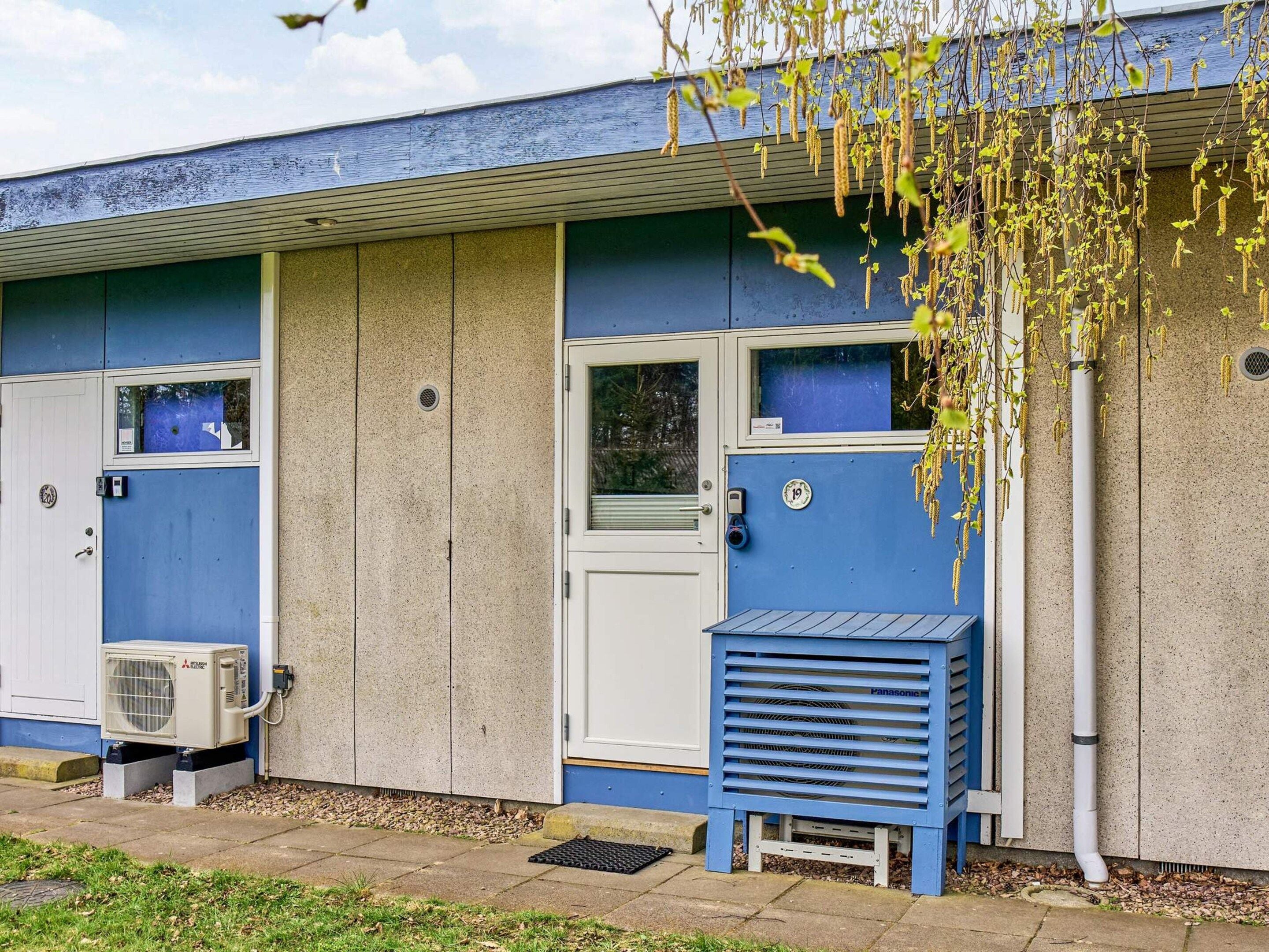 Um edifício com fachada azul e branca, uma porta com janela e uma pequena construção azul com ripas.