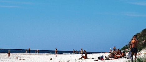 Uma praia com pessoas se banhando ao sol e um céu azul límpido.