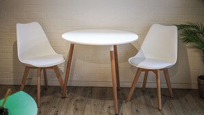 Duas cadeiras brancas com pernas de madeira e uma mesa redonda branca no meio.