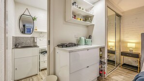 Cozinha compacta com armários brancos, pia, bancada com chaleira e um pequeno cesto de lixo.
