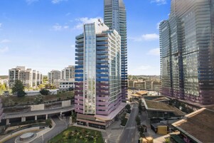 Um edifício moderno com fachada de vidro, rodeado por outros edifícios e um céu limpo.