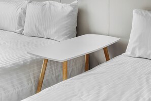 Uma cama bem arrumada com lençóis brancos e uma pequena mesa branca com pés de madeira em um quarto de hotel.