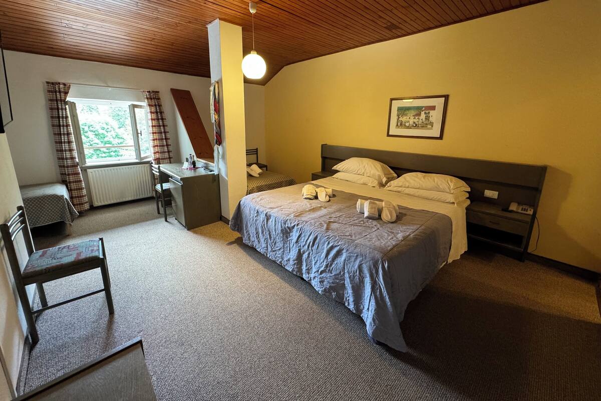 Quarto com cama, escrivaninha, cadeira, janela com cortinas e um quadro na parede.
