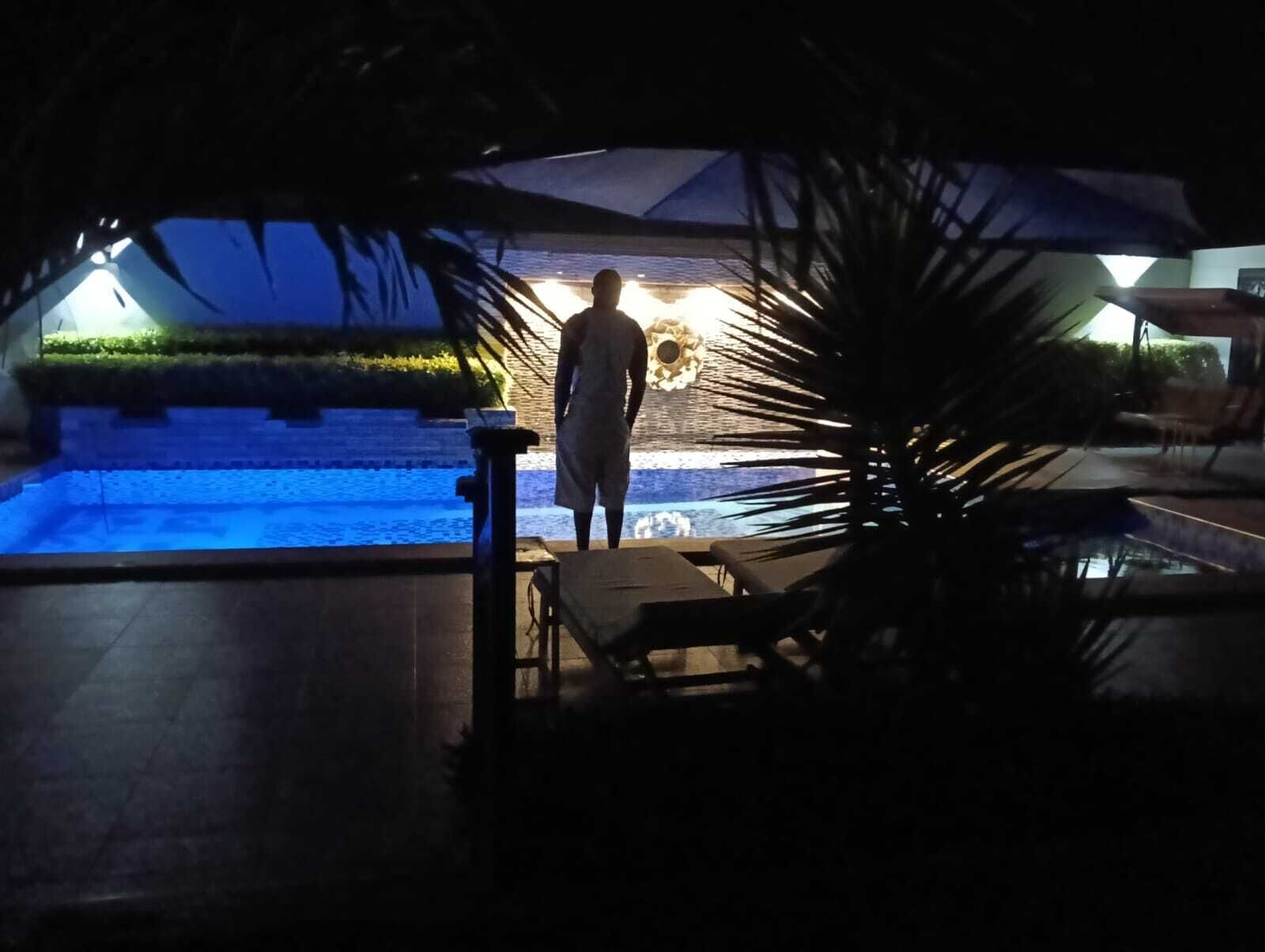 Uma pessoa parada perto de uma piscina, com vista para uma ponte e um pôr do sol.