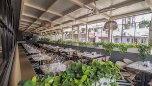 Restaurante com mesas internas, plantas penduradas e vista para a cidade.